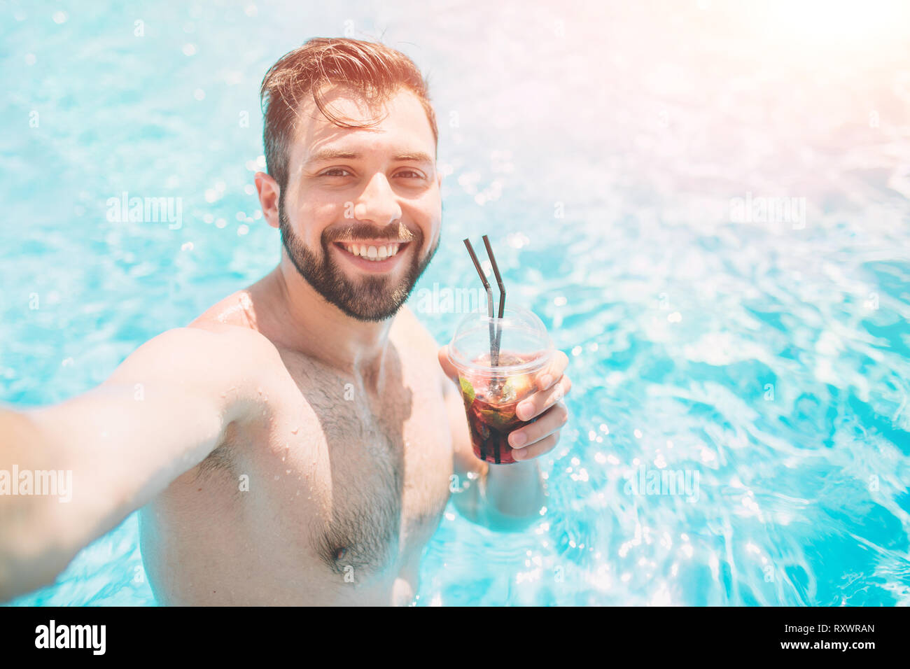 Happy bearded man making selfie in swimming pool. He is drinking a ...