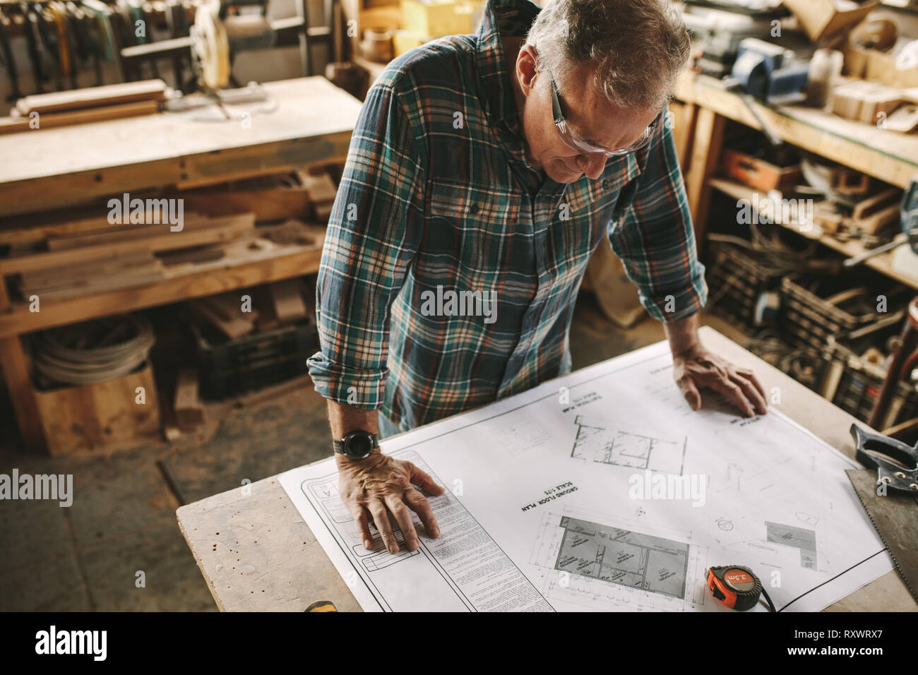 Senior carpenter studying blueprint at his workshop before starting his ...