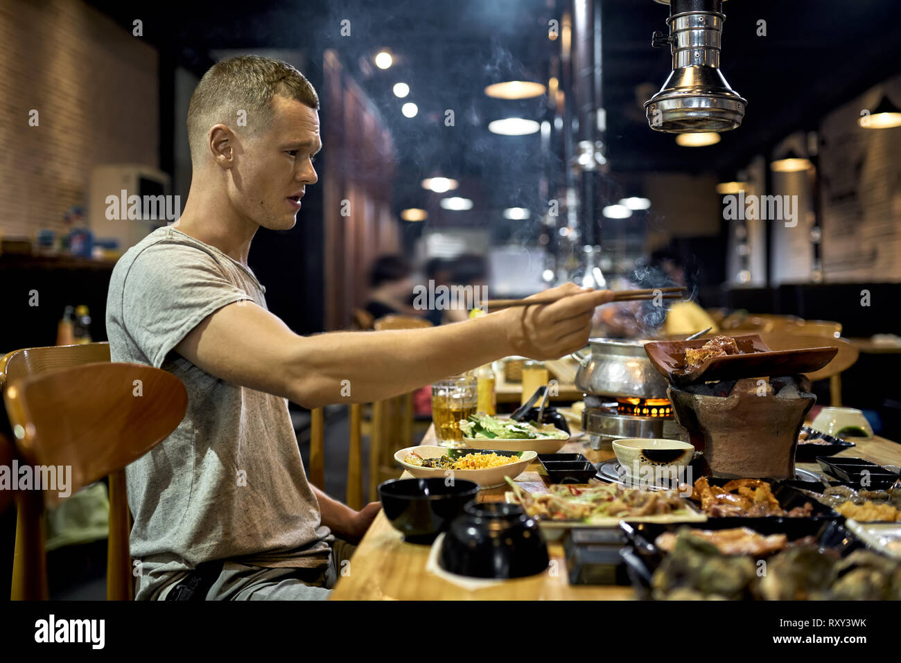 Cute guy with chopsticks is sitting by the wooden table and cooking ...