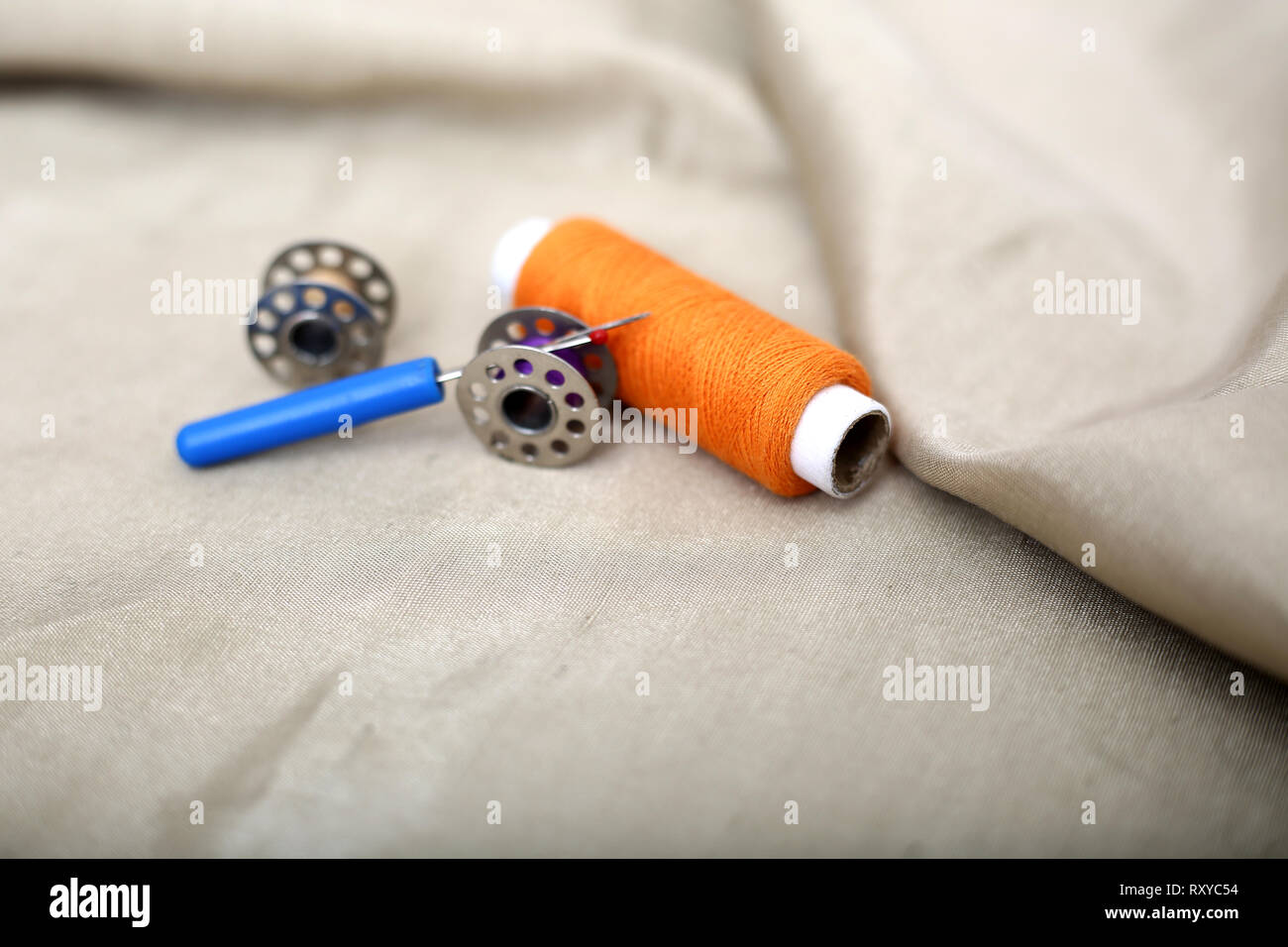 Photo of orange sewing thread, needle ripper and two bobbin on the ...