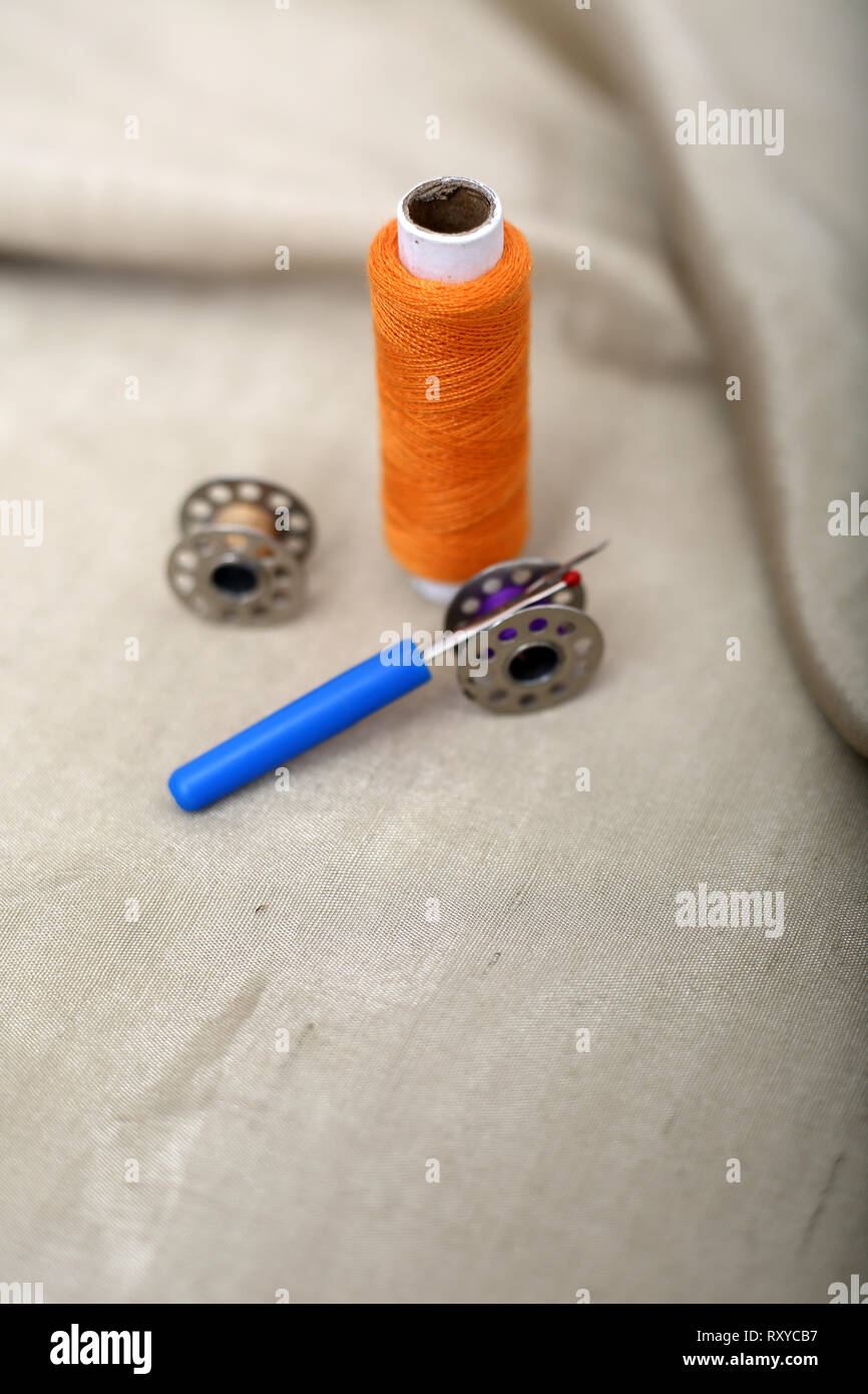 Picture of one orange thread, needle ripper and bobbin on the cloth ...