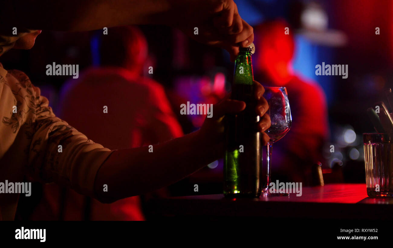 Bar with neon lighting. A man opens up a beer bottle. Mid shot Stock ...