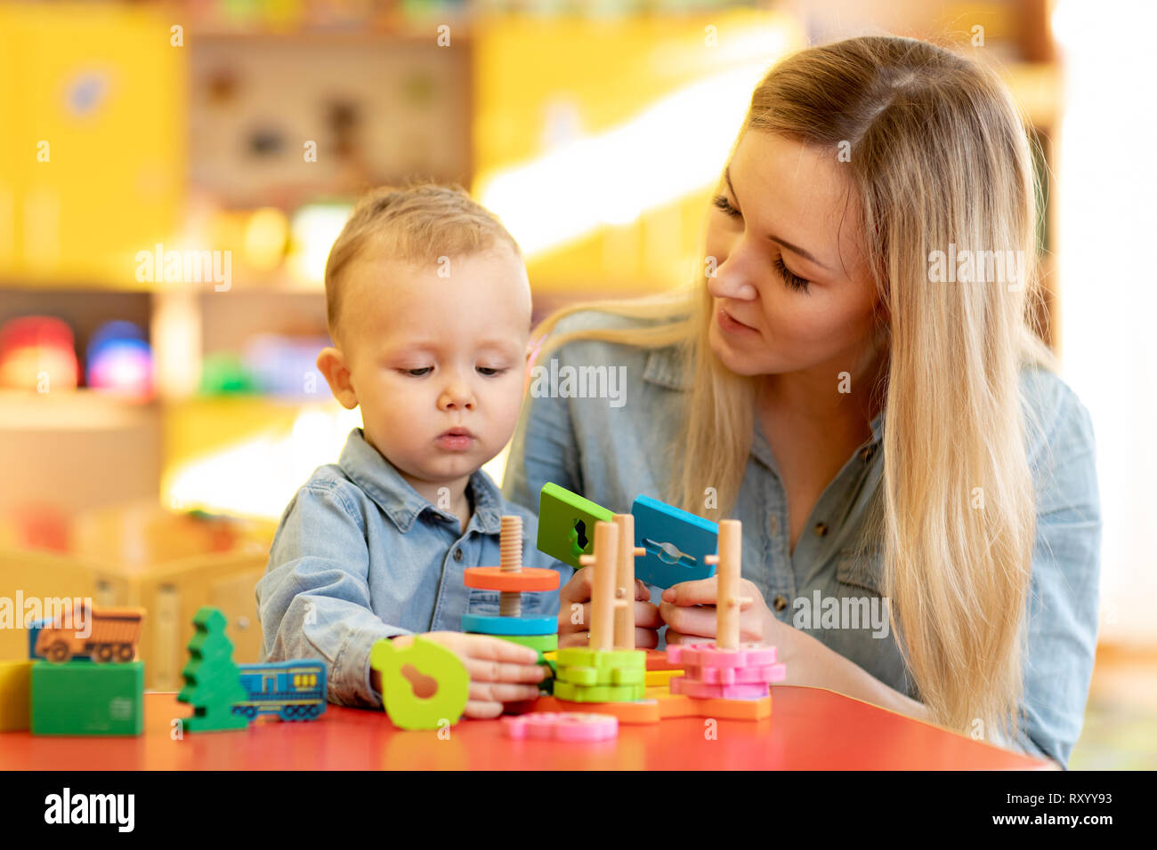 Baby minder playing with kid in nursery. Developmental toys for ...