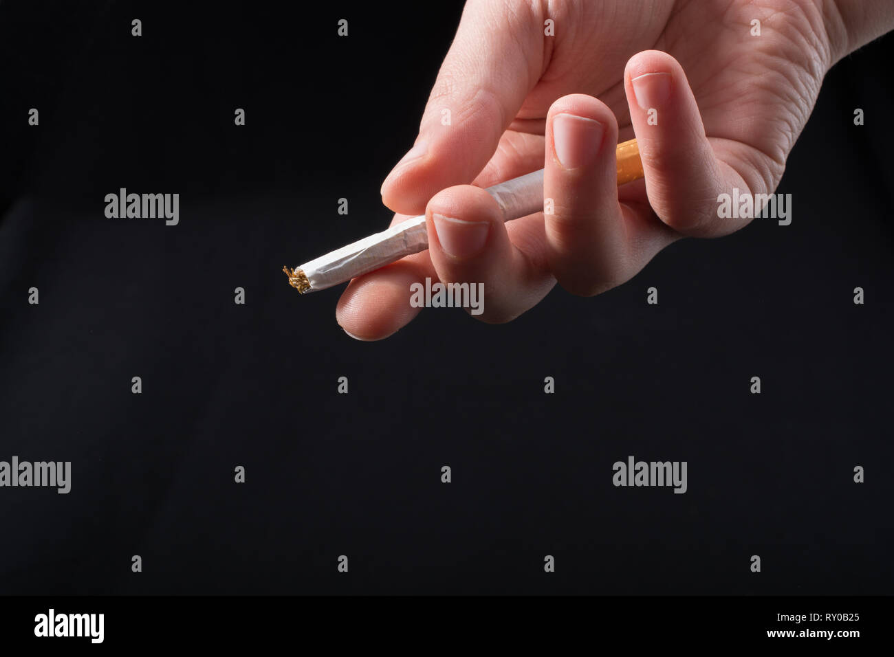 Hand is giving out cigarette on a black background Stock Photo - Alamy