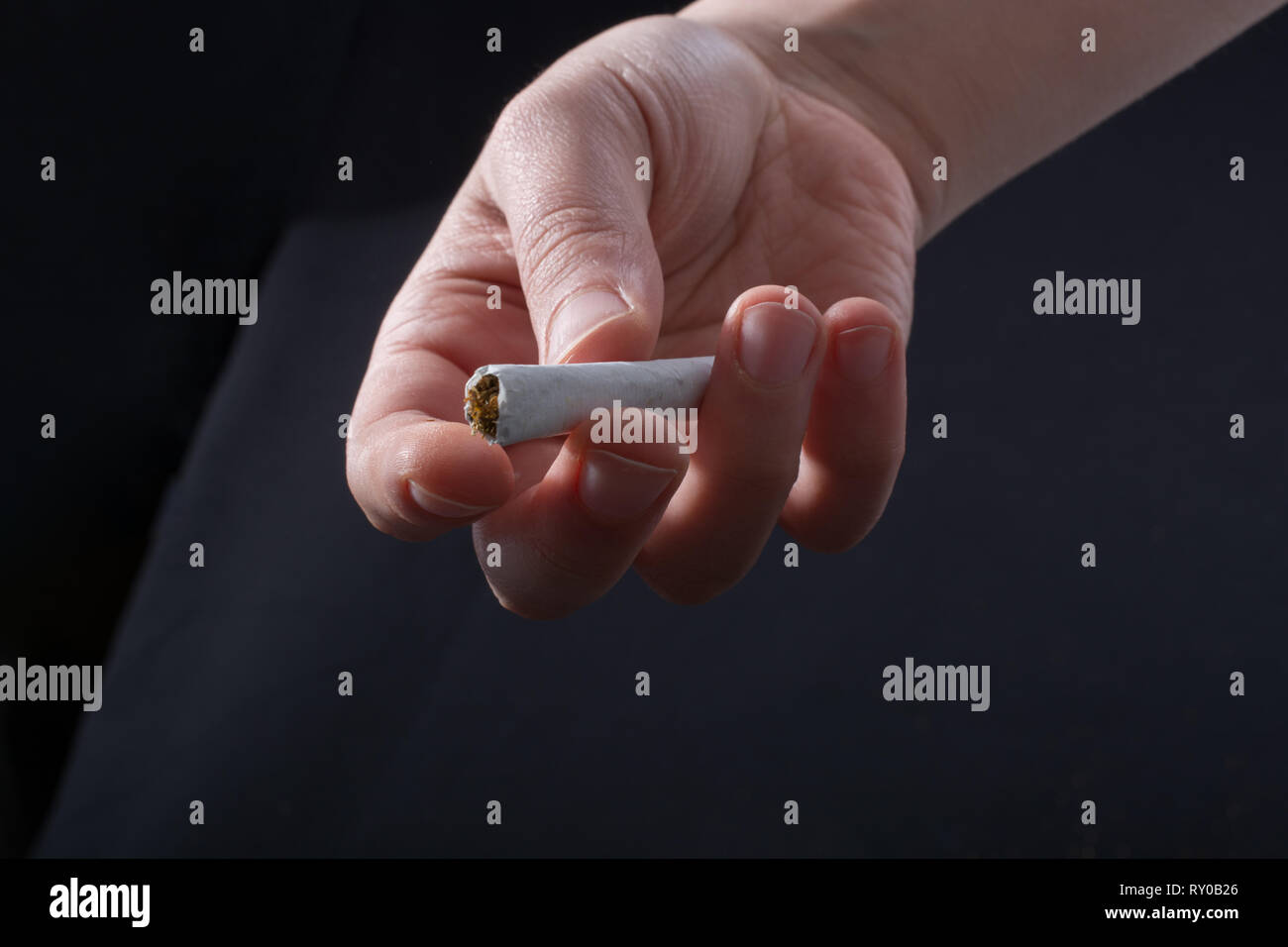 Hand is giving out cigarette on a black background Stock Photo - Alamy