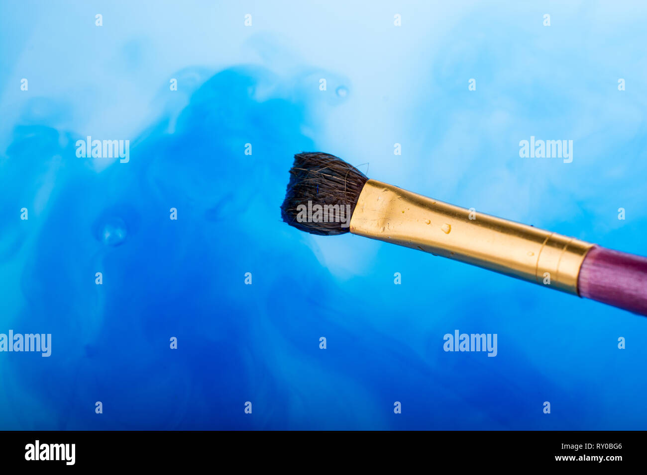 Watercolor paint dissolving in water as painting brush touches water ...