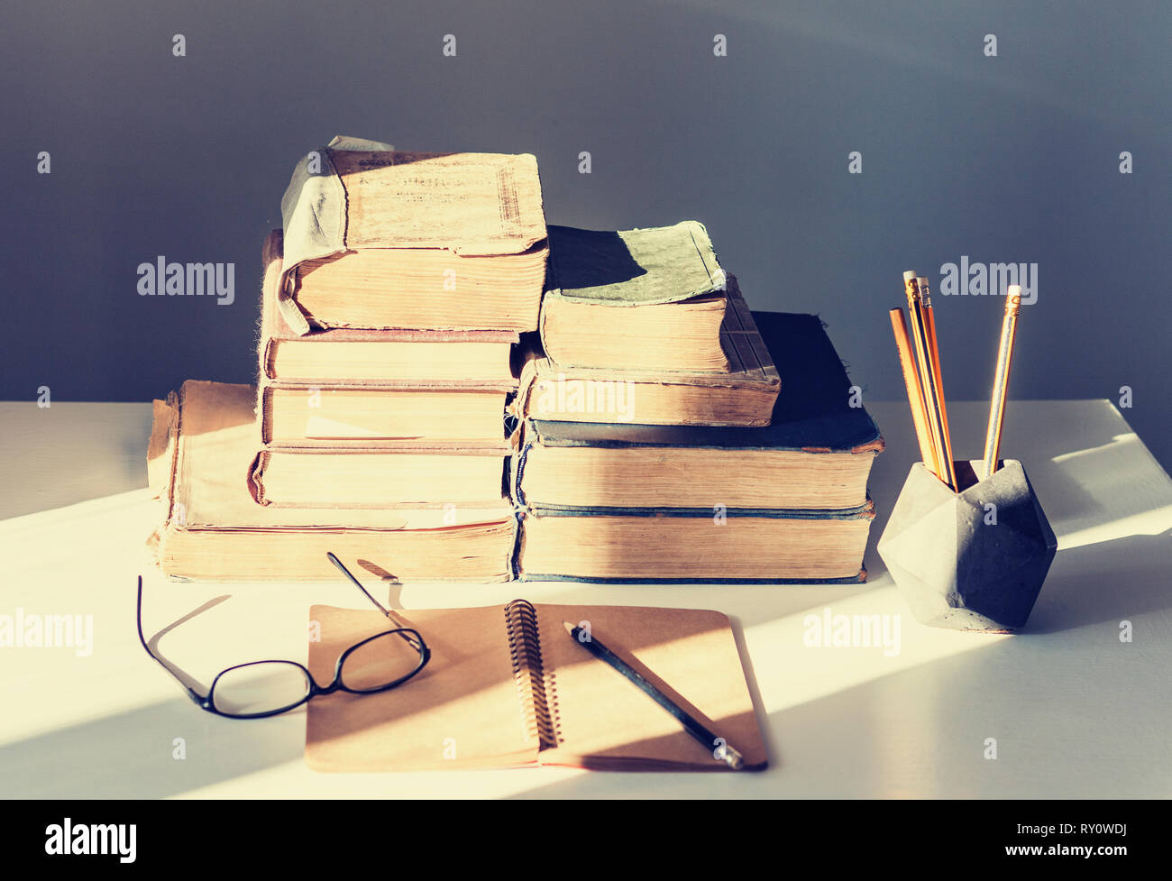 Stack of old books, textbook, glasses and pencils in office background ...