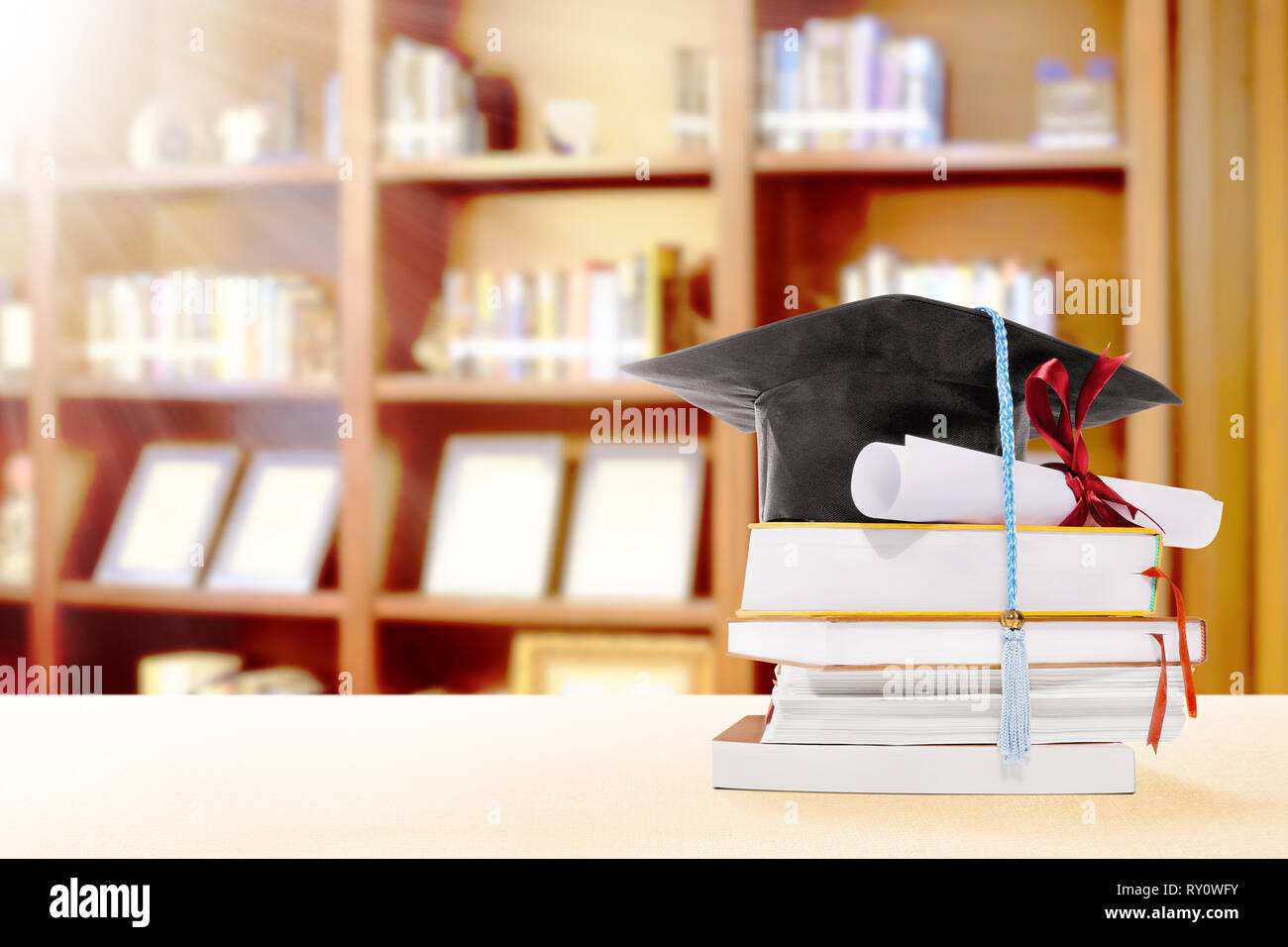 Graduation hat, diploma scroll and books on the table with bookshelf on ...