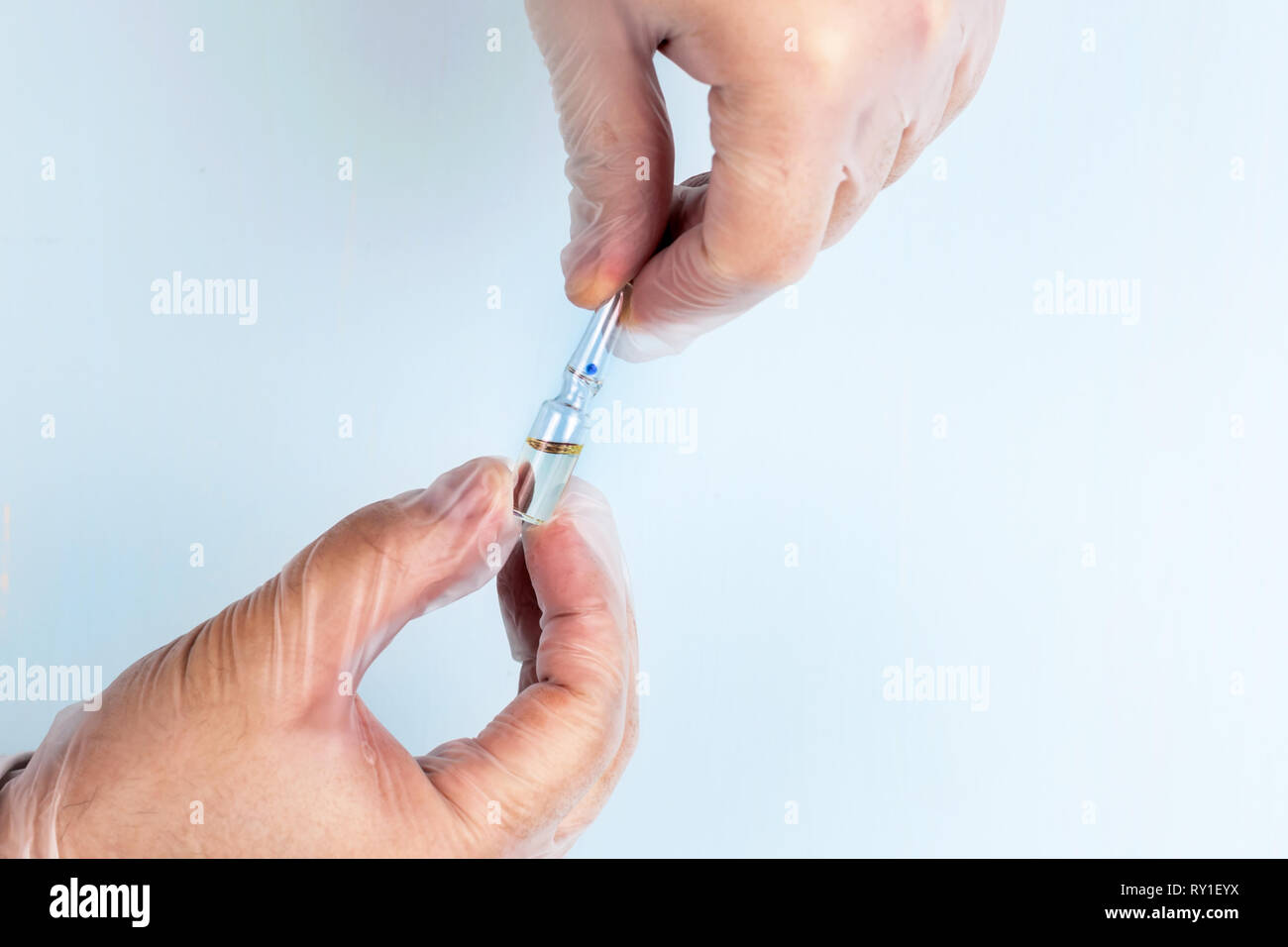 Male hand in a transparent medical nitrile glove holds a vial of ...
