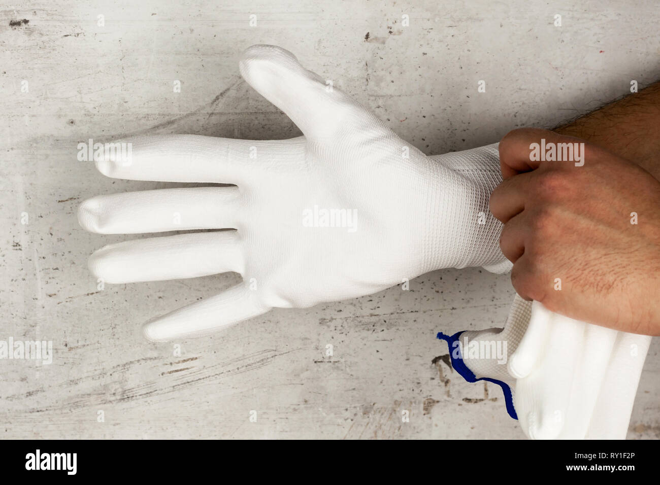 A man puts on a glove on his hand for repairs. Hand on light concrete ...