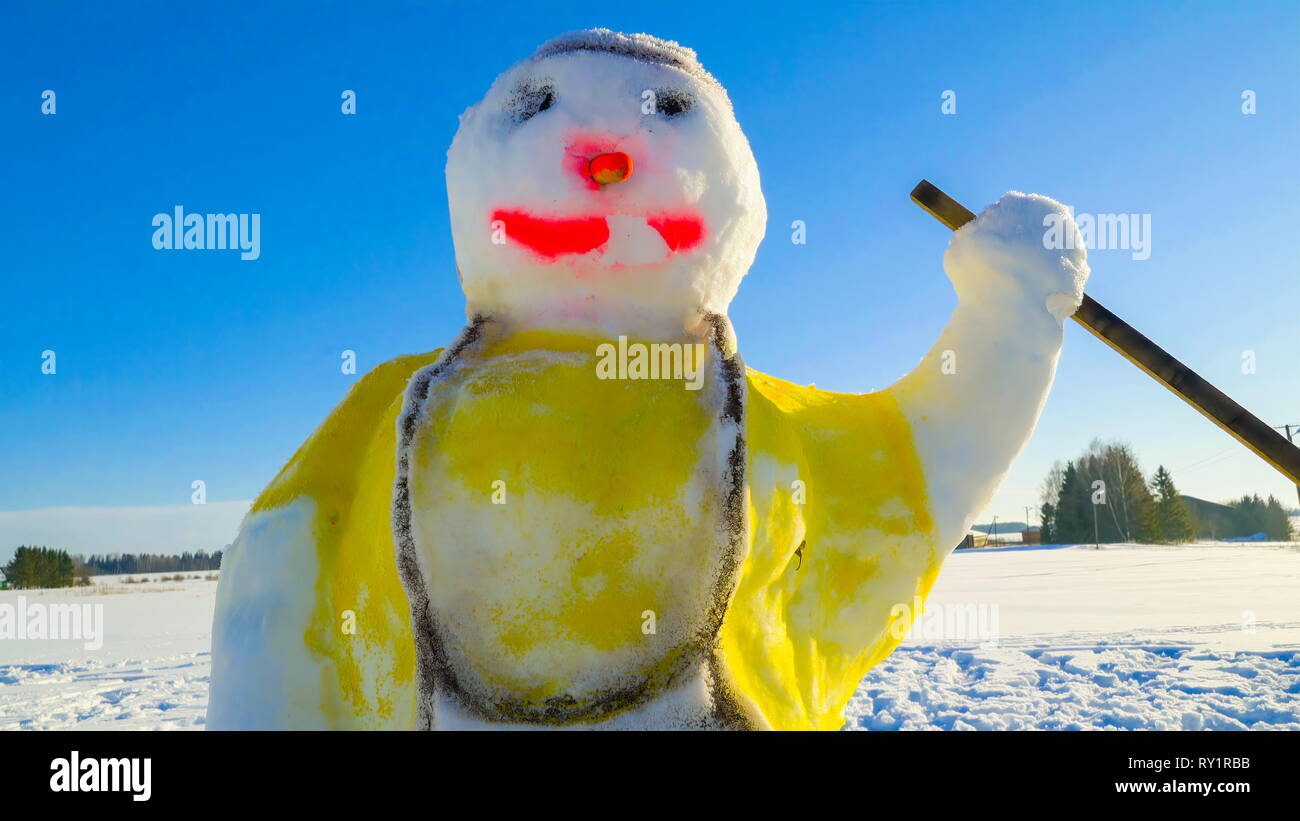 A colorful snowman with yellow shirt on it. The snowman has a long nose ...