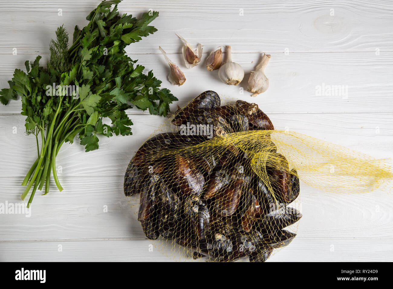 Fresh raw mussels in a grid with parsley and garlic on white wood ...