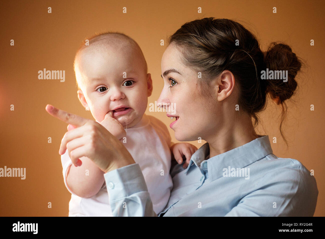 young woman hugging a baby on an orange background Stock Photo - Alamy