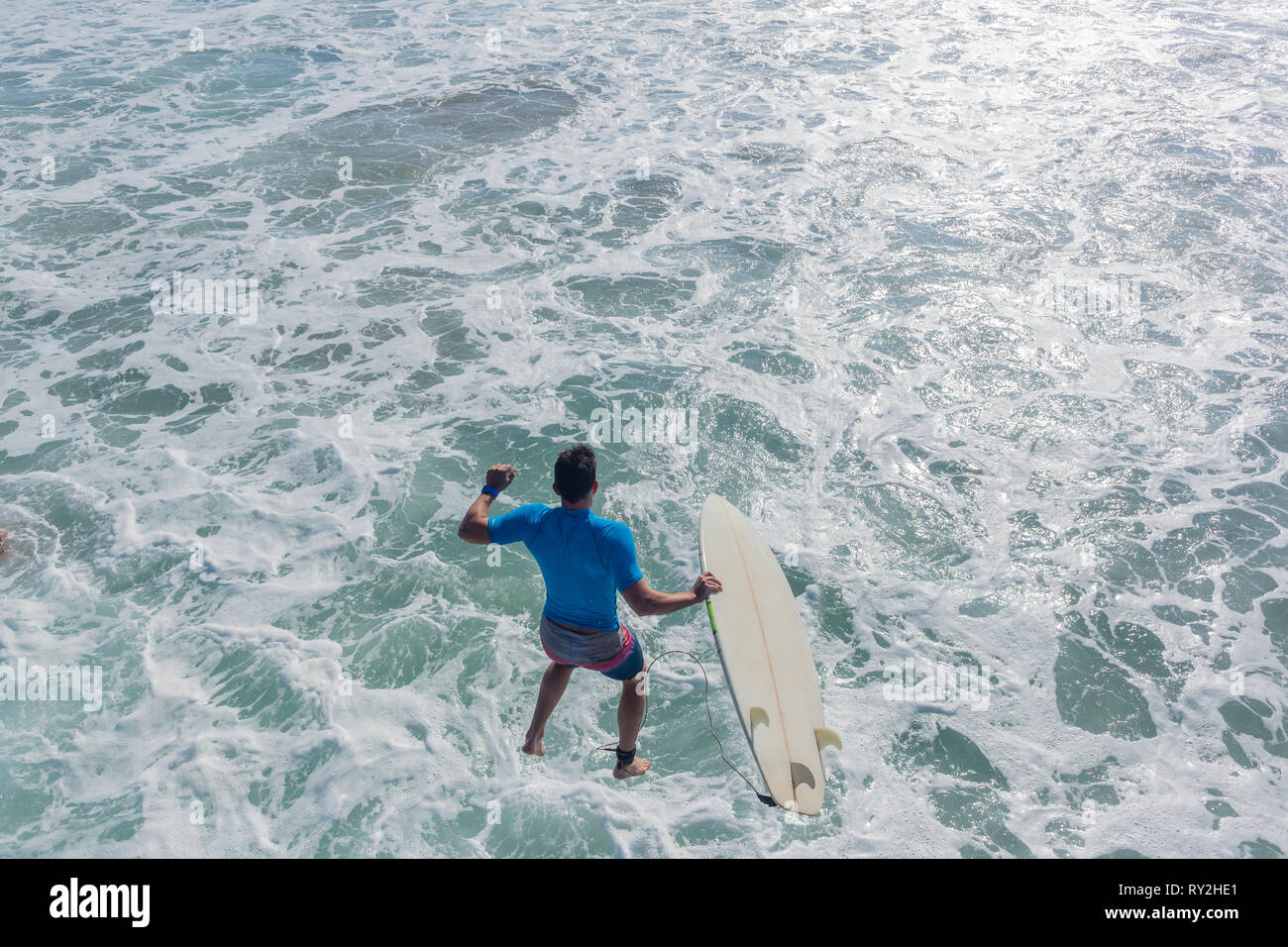 Surfer with surfboard jumps beach pier jetty into ocean water for quick ...