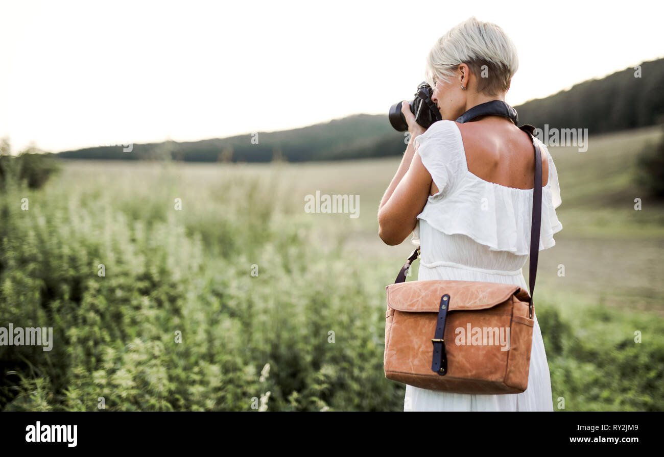 A rear view of woman photographer with a leather bag and camera in ...
