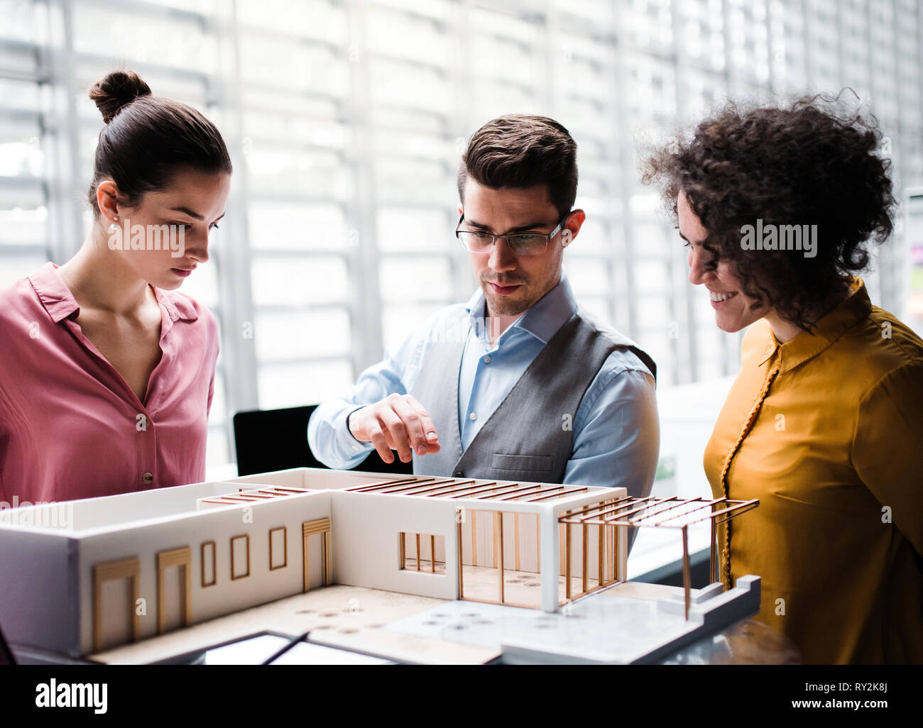 A group of young architects with model of a house standing in office ...