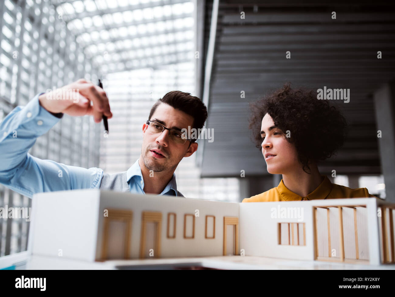 Two young architects with model of a house standing in office, working ...