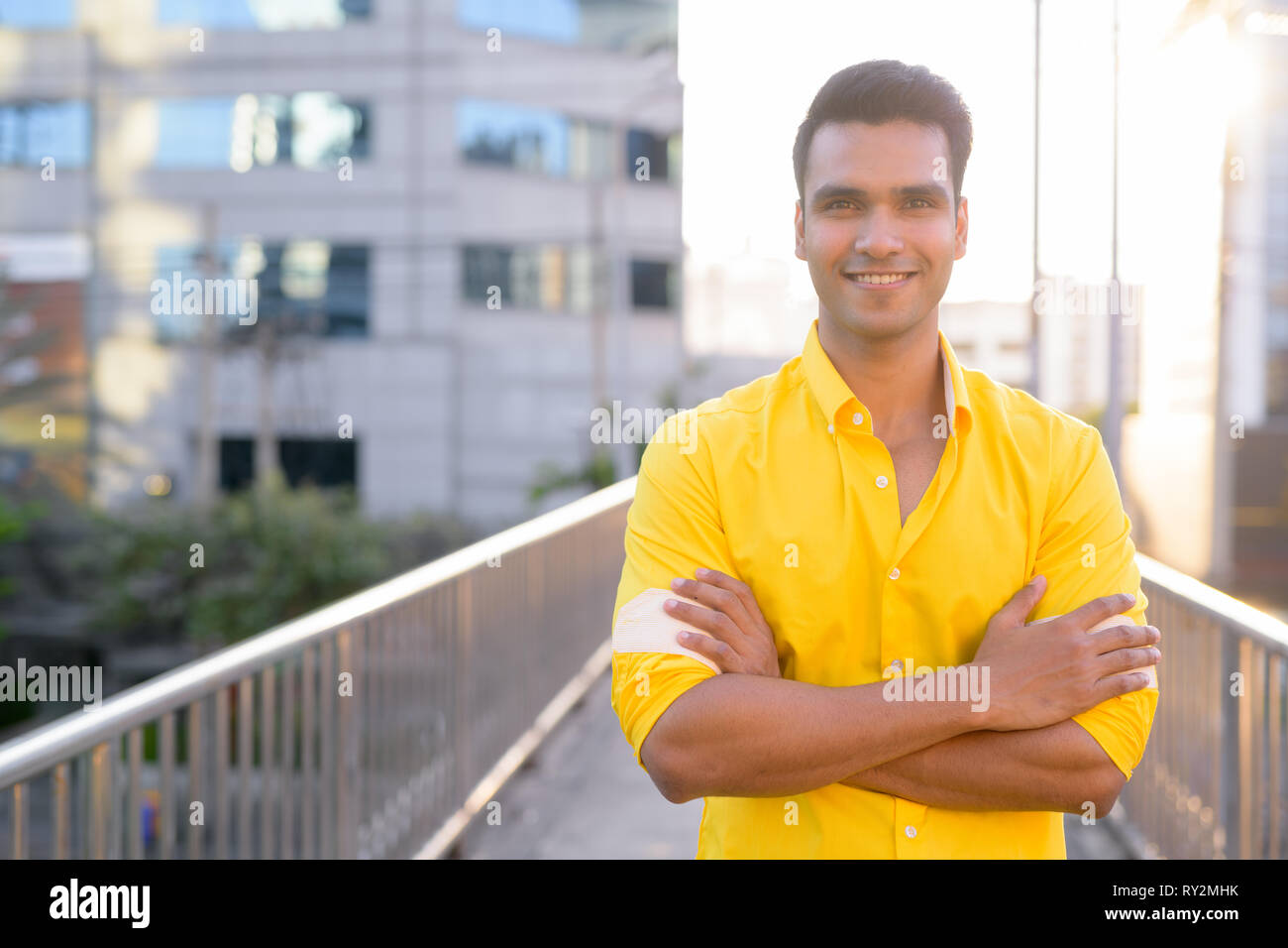 Happy young handsome Indian man smiling with arms crossed on the ...
