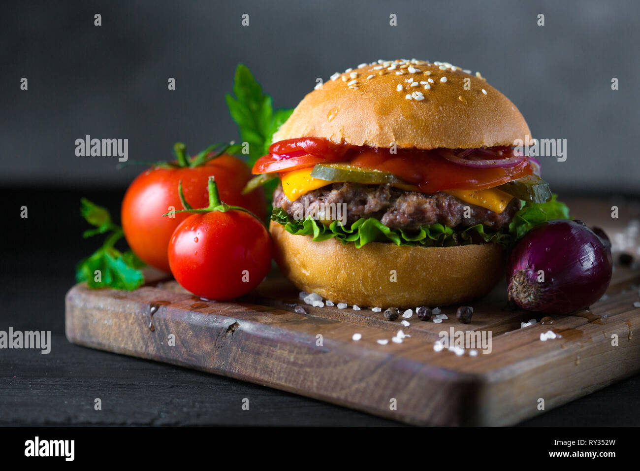 Classic american cheeseburger on a wooden board with tomatoes and onion ...