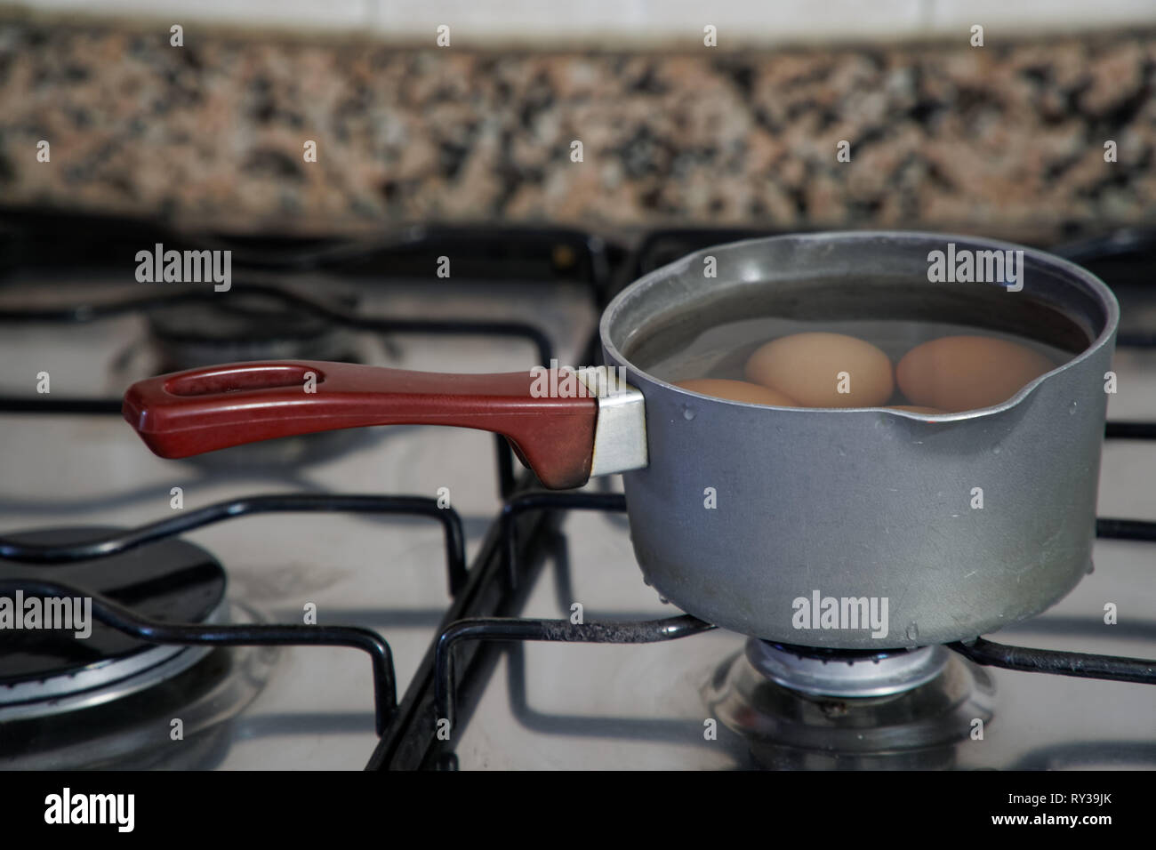 Boiled eggs in dipper of water on the kitchen stove Stock Photo - Alamy