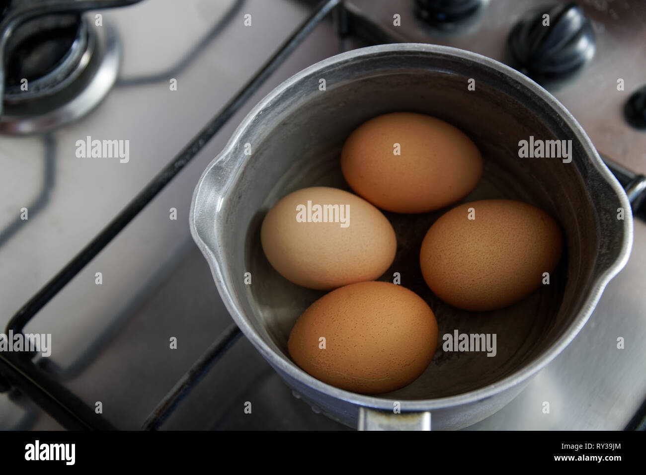 Boiled eggs in dipper of water on the kitchen stove Stock Photo - Alamy