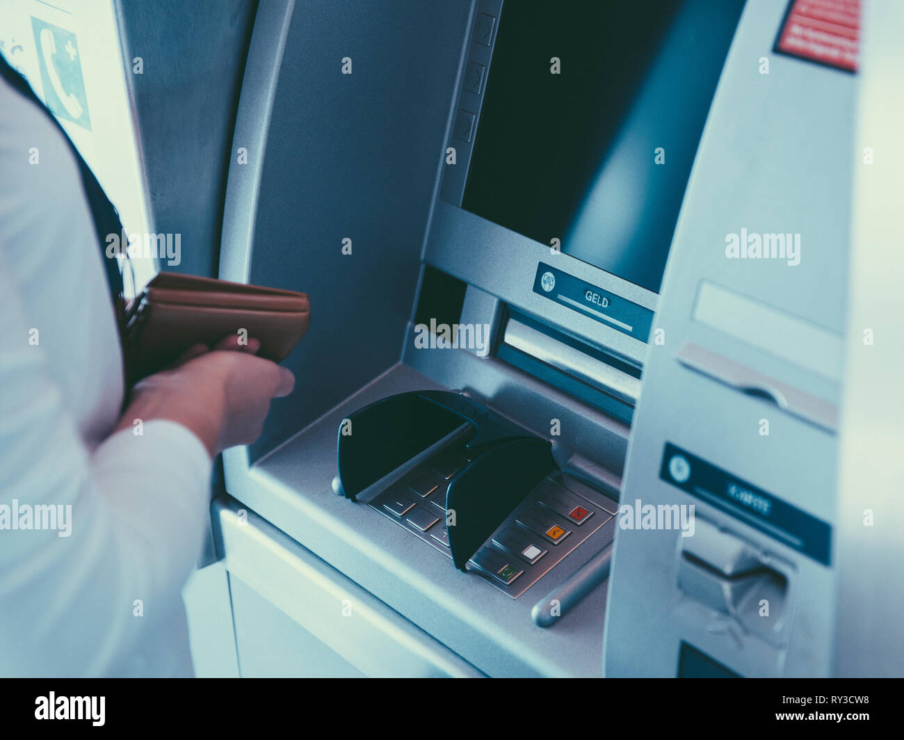 Side view of woman using ATM Automatic Teller Machine cash machine to enter the security PIN and ...