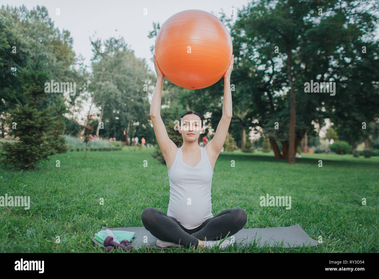 Concentrated young woman sit in lotus pose on yoga mate in park. She ...