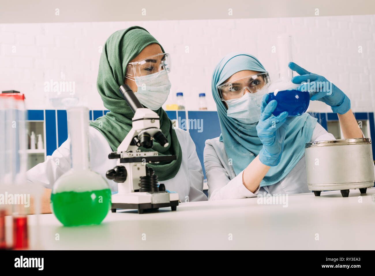 female muslim scientists with flasks and microscope during experiment ...