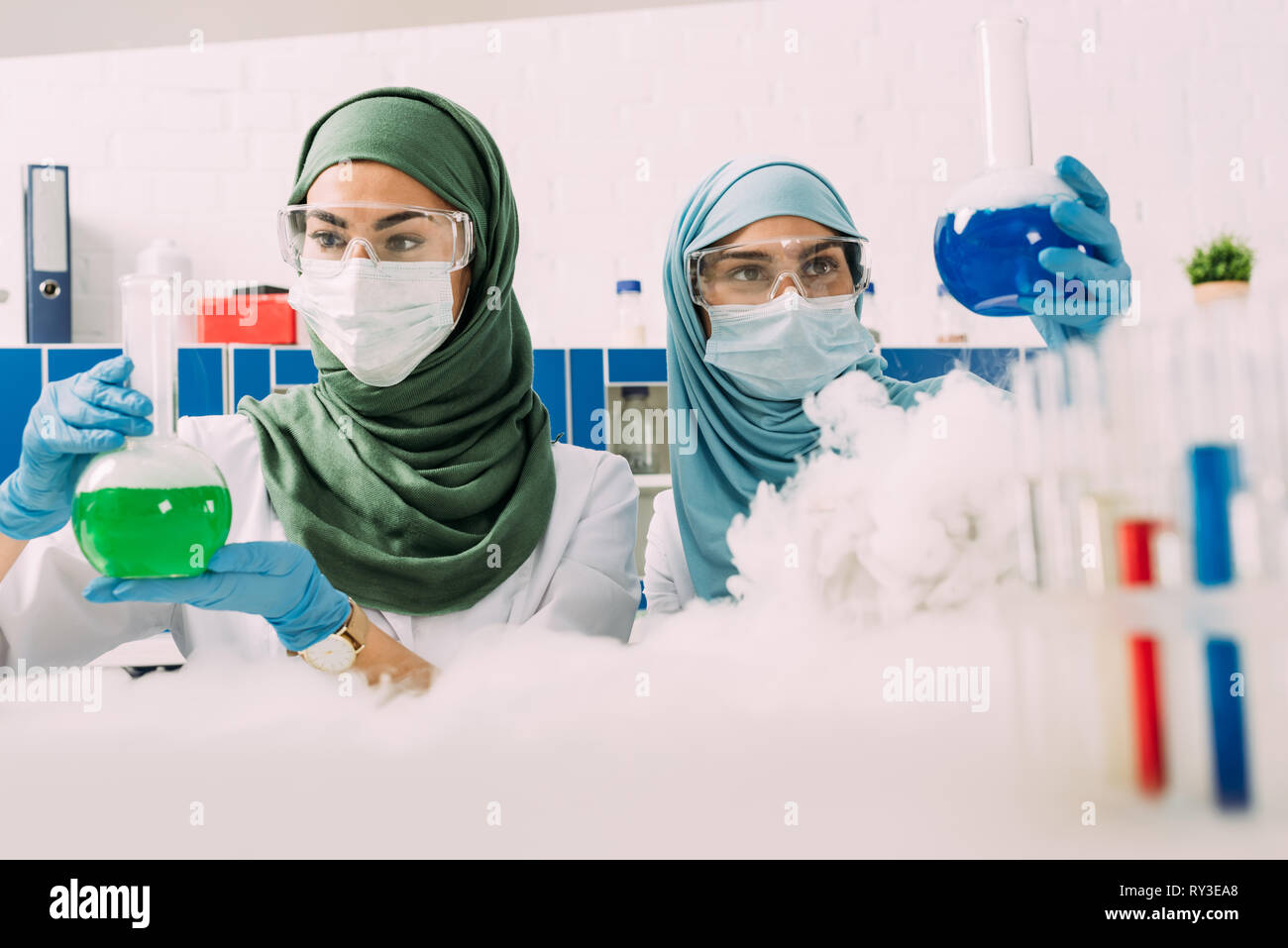 female muslim scientists holding flasks while experimenting with dry ...
