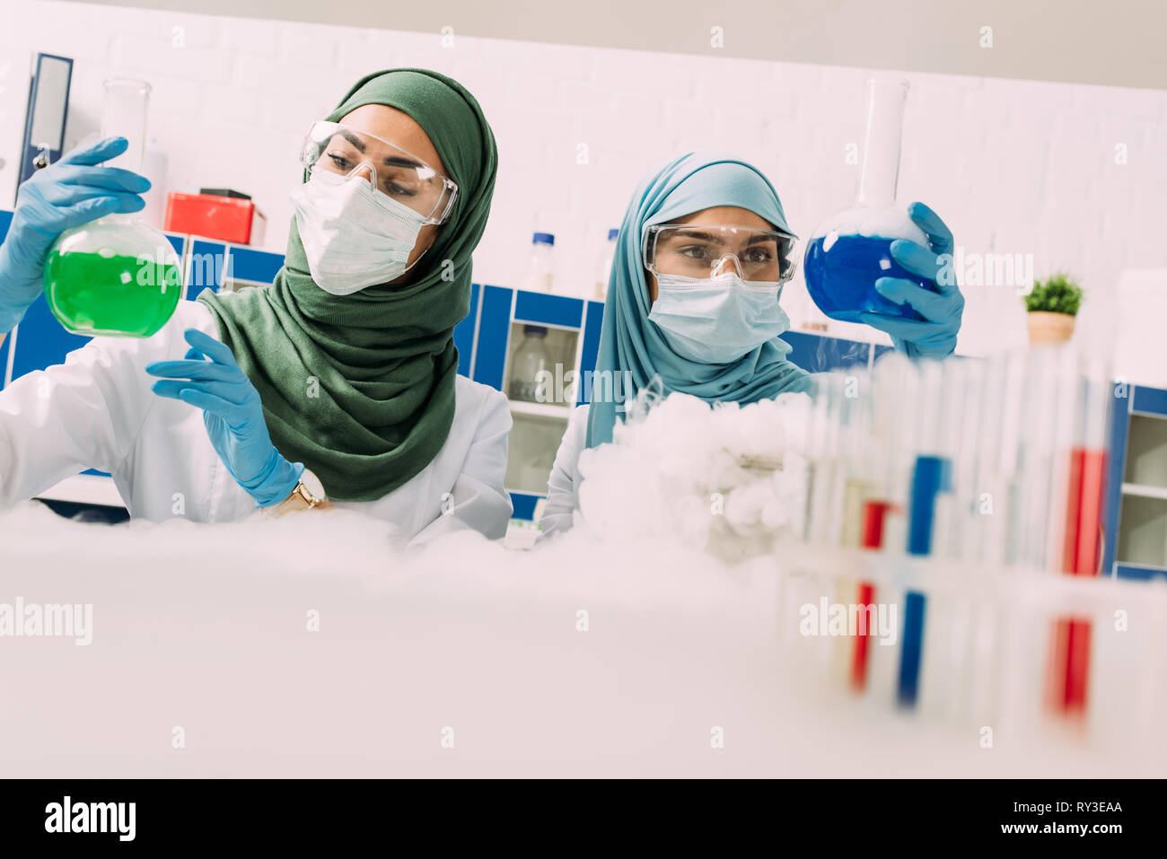 female muslim scientists in medical masks holding flasks while ...