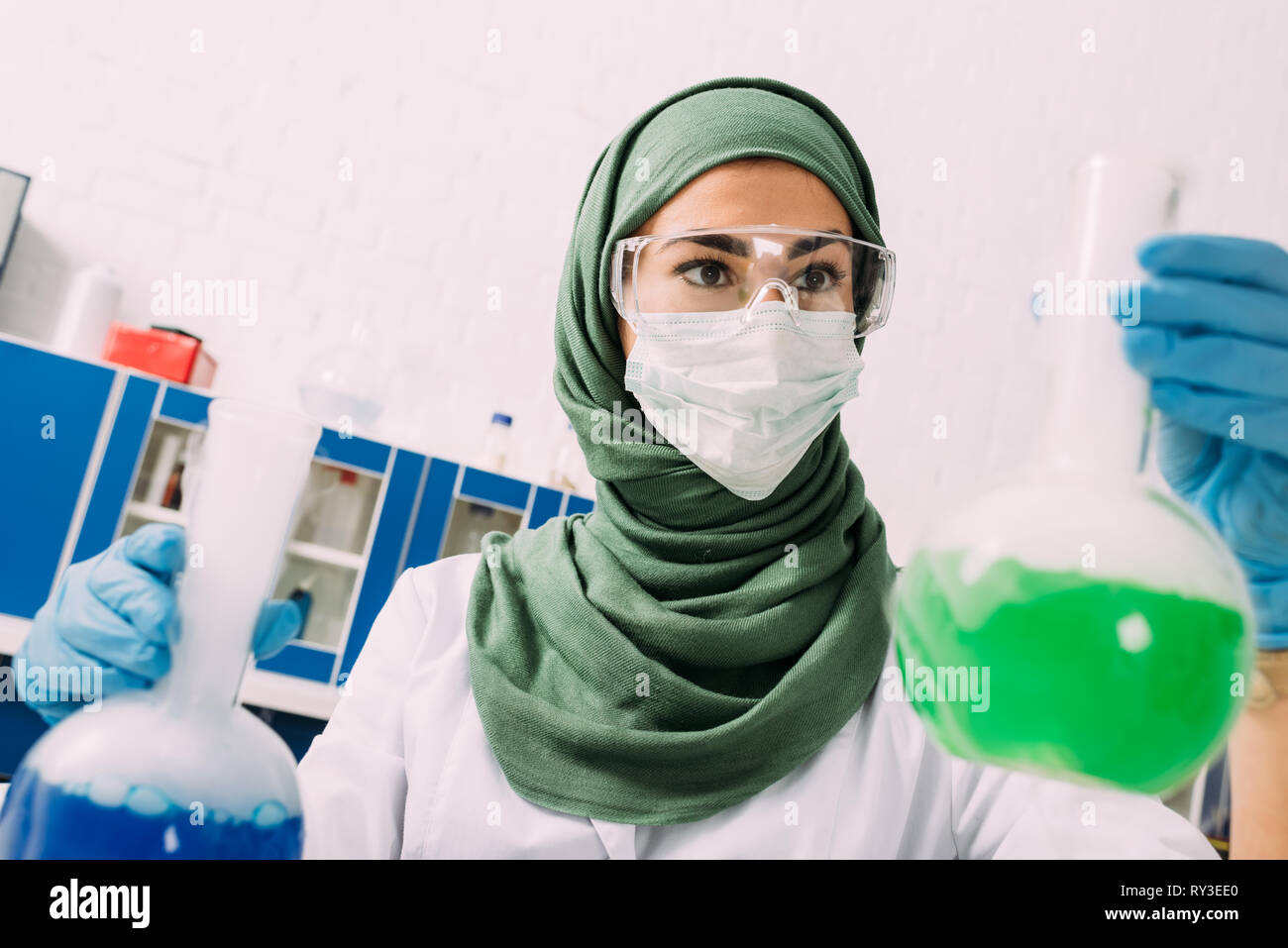 female muslim scientist holding flasks during experiment in chemical ...