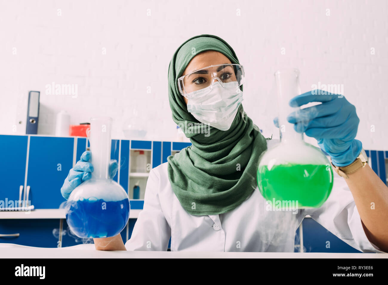 female muslim scientist in medical mask holding flasks during ...
