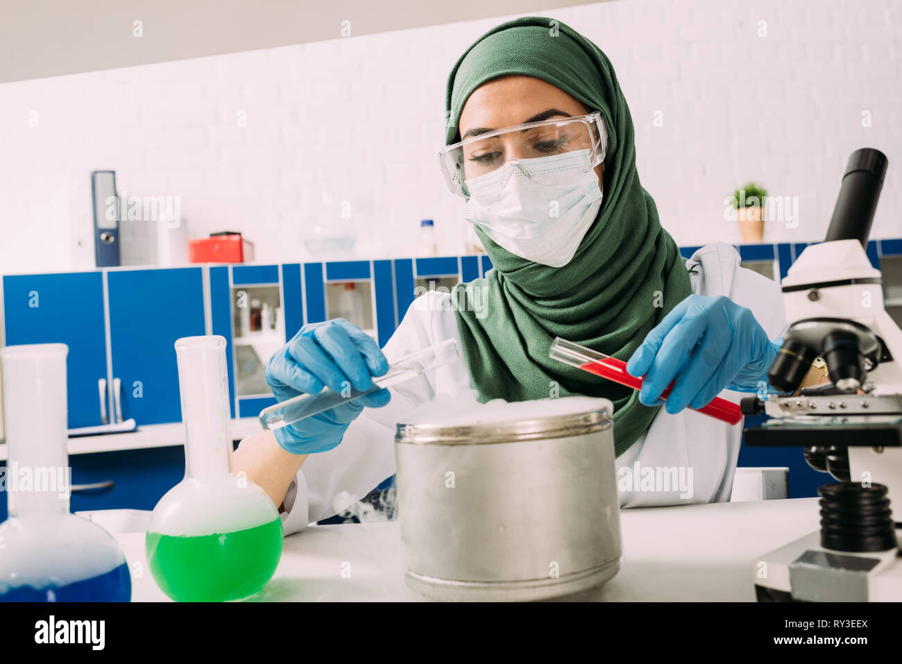 female muslim scientist holding test tubes over pot with dry ice during ...