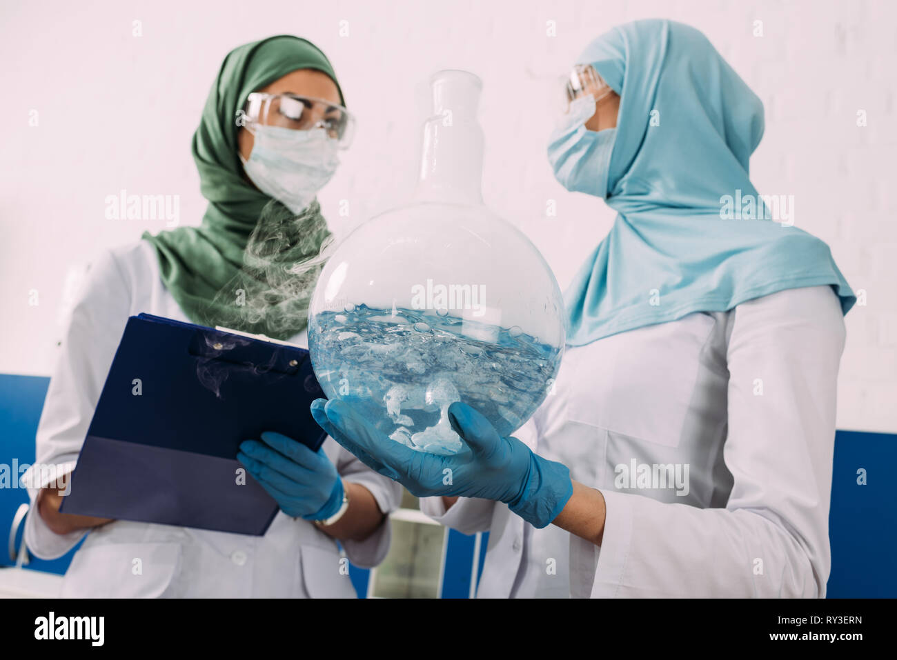 female muslim scientists holding clipboard and flask wth liquid in ...