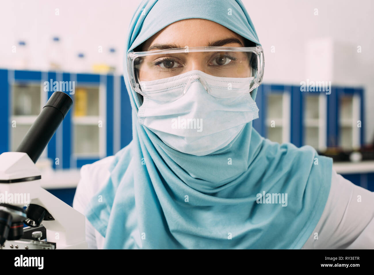 female muslim scientist in medical mask, goggles and hijab looking at ...