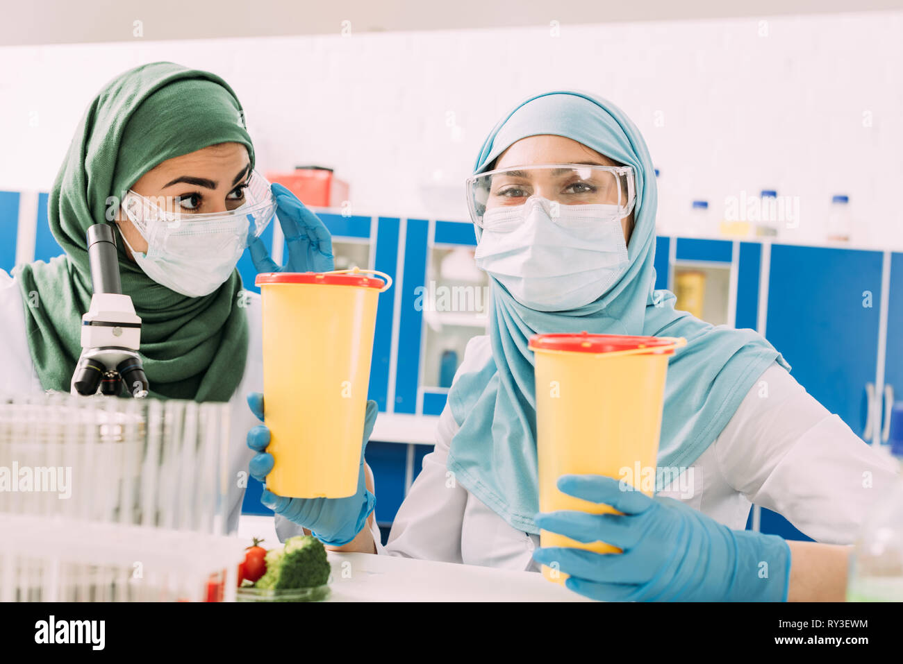female muslim scientists holding clinical waste containers and looking ...
