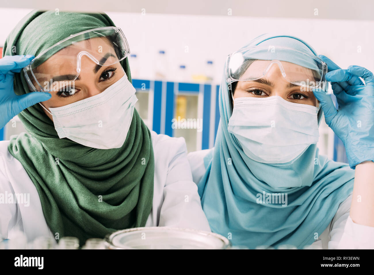 female muslim chemists in medical masks and hijab looking at camera in laboratory Stock Photo ...