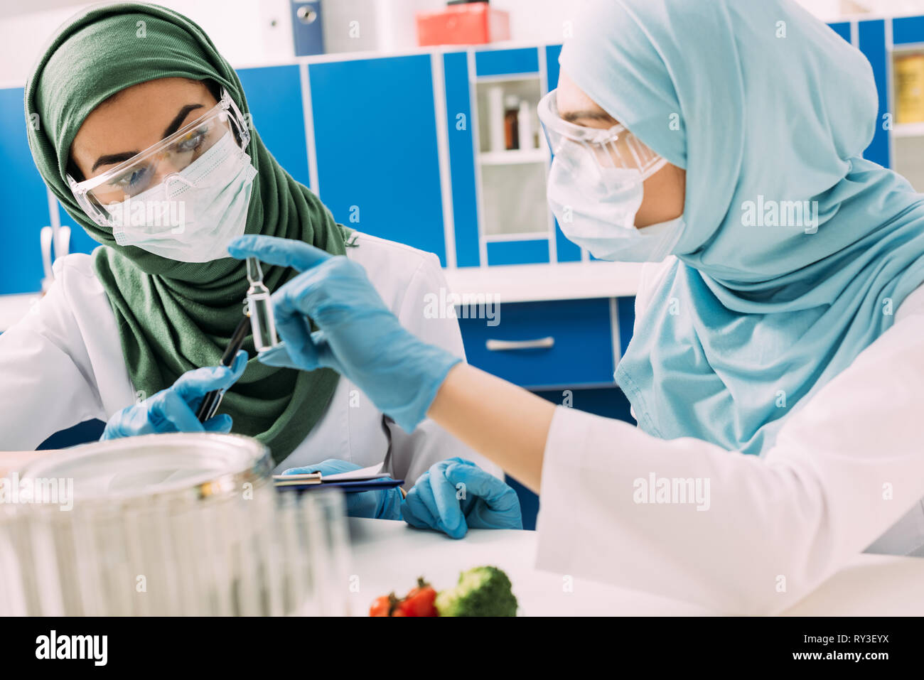 female muslim scientists in medical masks holding glass ampoule during ...