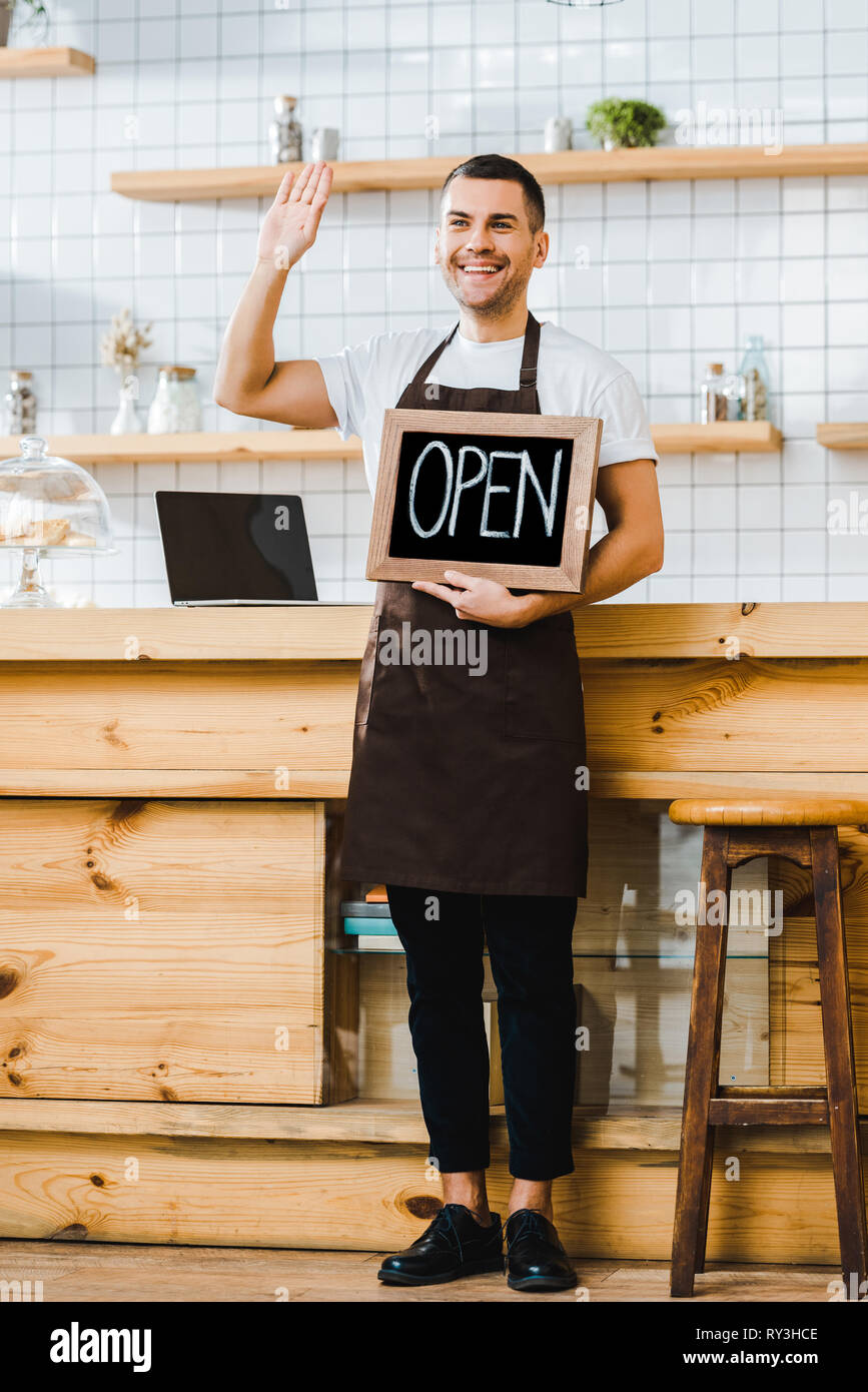 handsome cashier standing near wooden bar counter, holding chalkboard ...