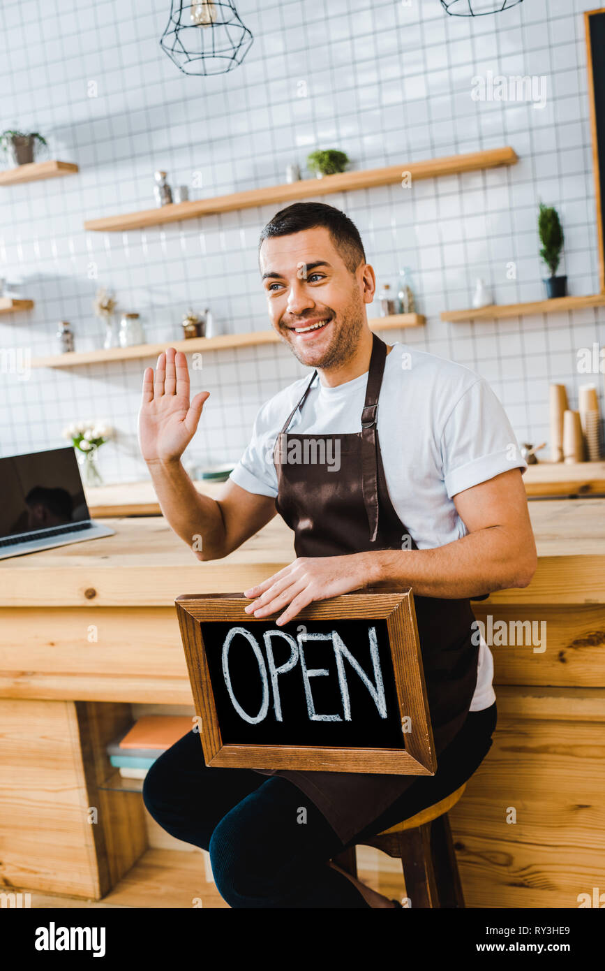 handsome cashier in apron sitting on chair near wooden bar counter ...
