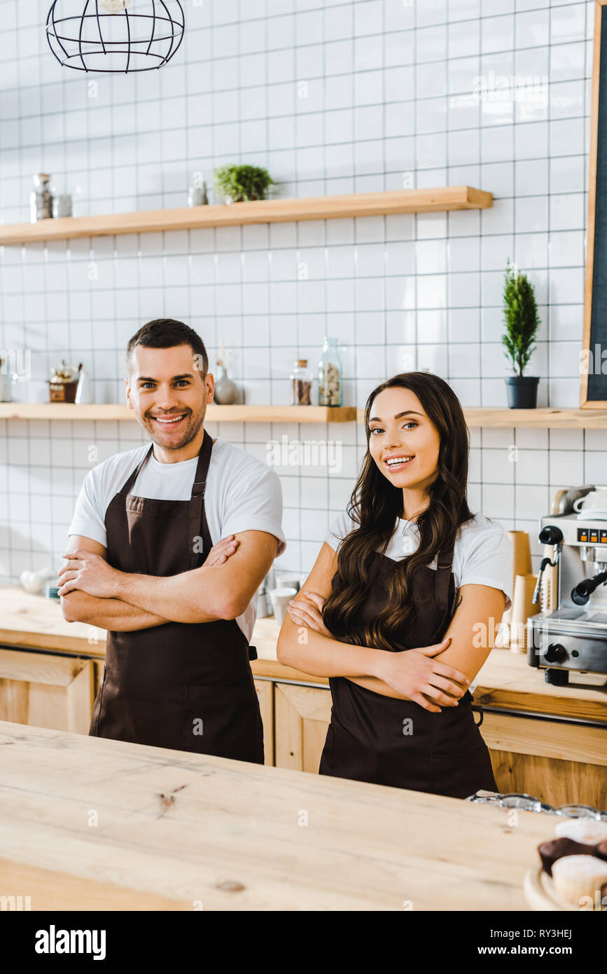 cashiers smiling and standing behind wooden bar counter in coffee house ...
