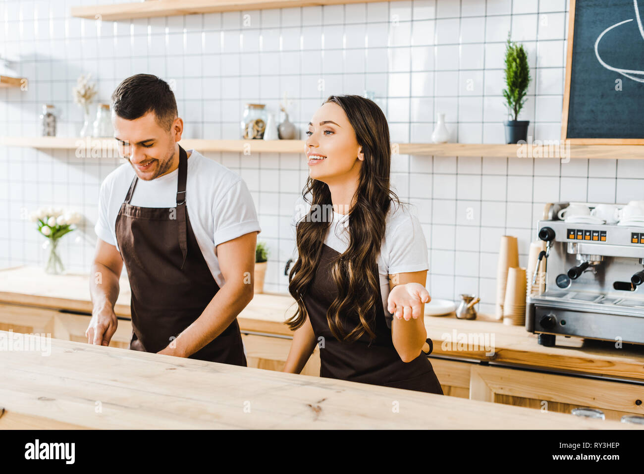 attractive cashier standing behind wooden bar counter and smiling wile ...