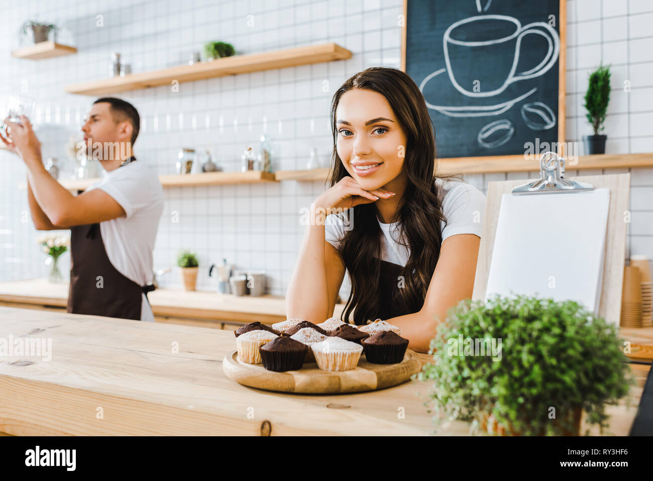 attractive brunette waitress standing behind bar with cupcakes on ...