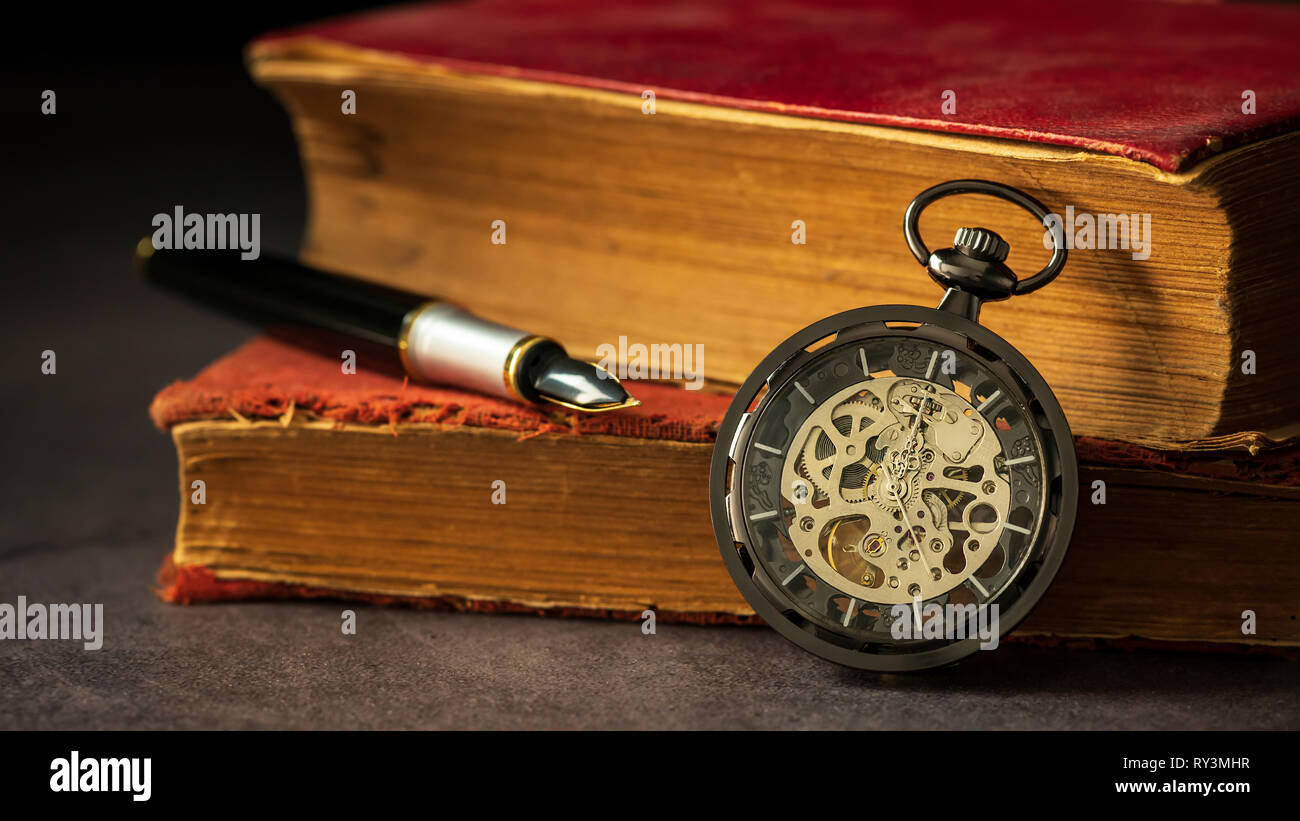 Winding pocket watch placed beside the old book and the pen on the book ...