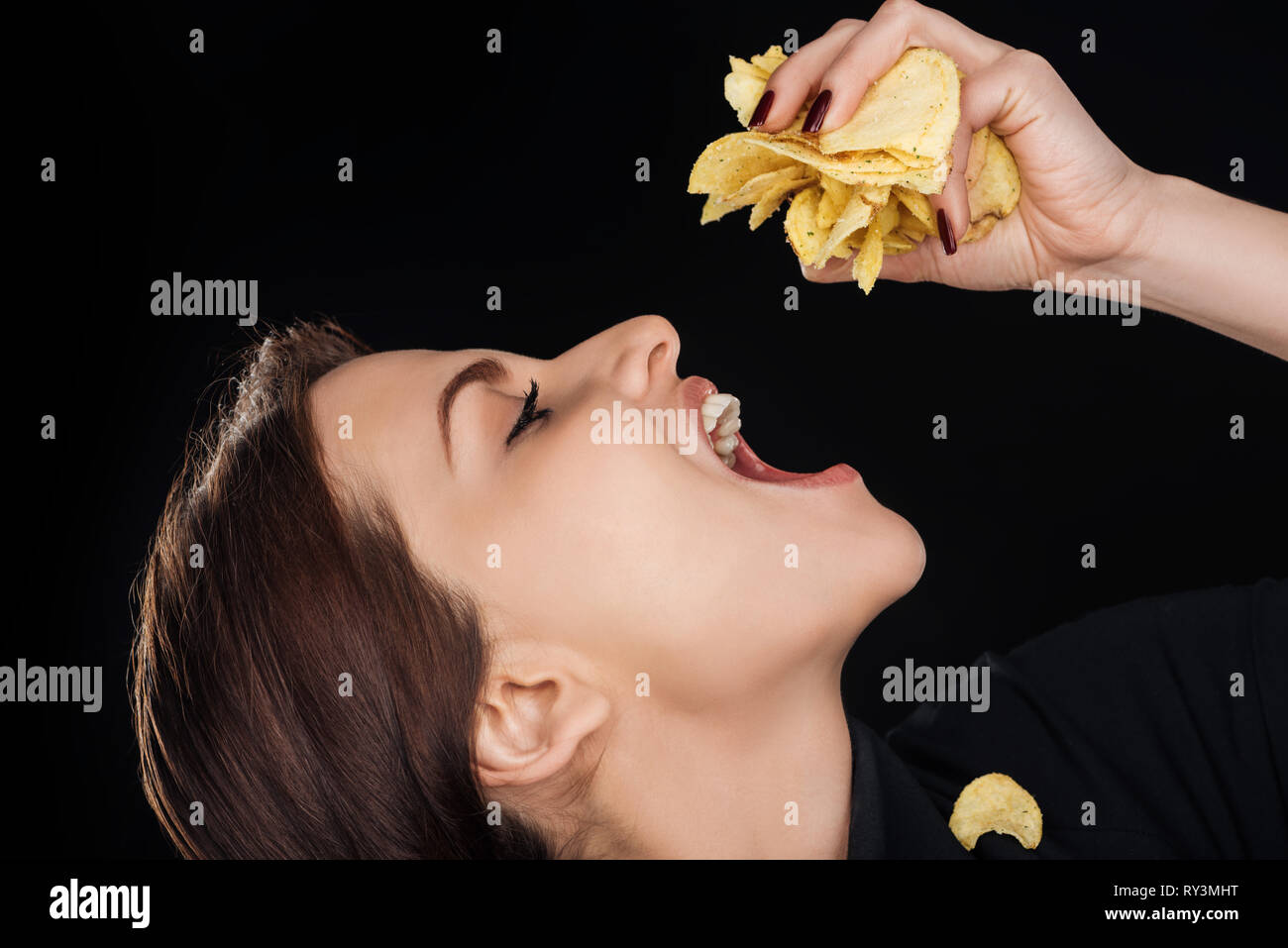 beautiful woman eating crispy chips isolated on black Stock Photo - Alamy