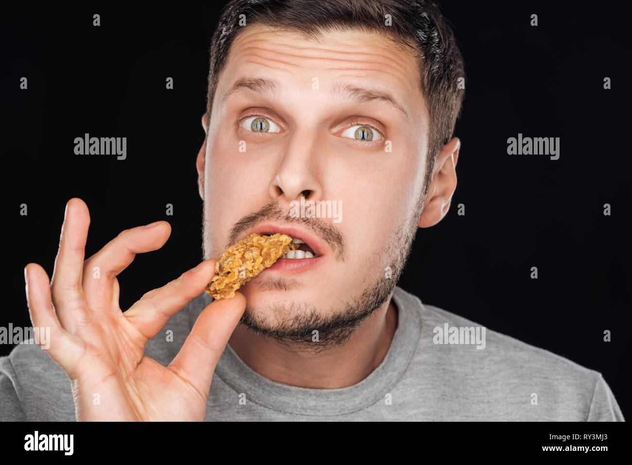 handsome man eating chicken nugget while looking at camera isolated on ...