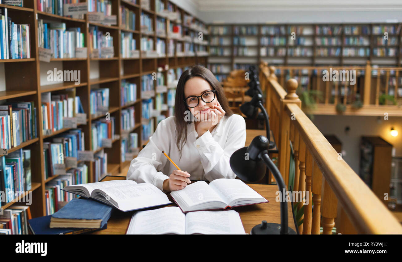 Brunette female student with books working in a high school library ...