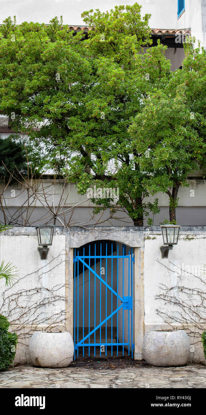 Entrance gate in the Greek courtyard behind a white high wall. Vertical ...