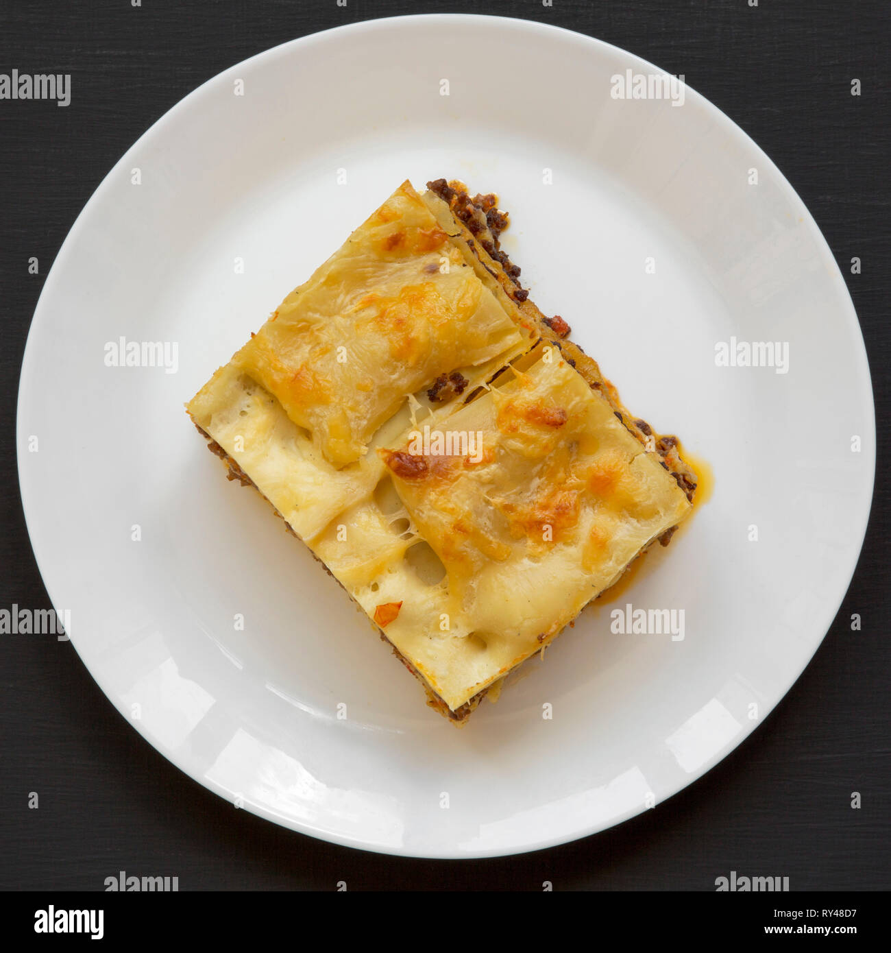 Traditional beef lasagne on a white round plate on black table, top ...