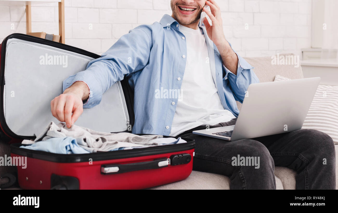 Travel alone. Man talking on phone and packing clothes Stock Photo - Alamy